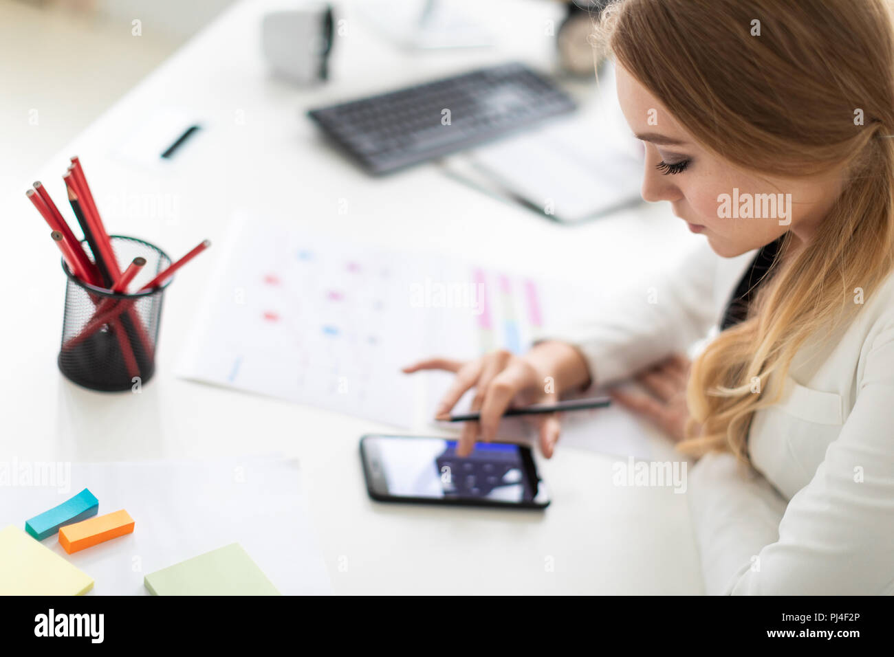 A young girl sits at a computer desk in the office and counts on a ...