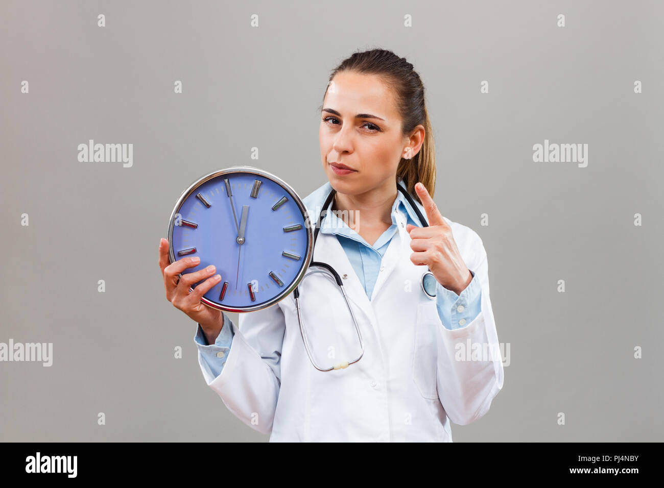 Serious female doctor holding clock Stock Photo - Alamy