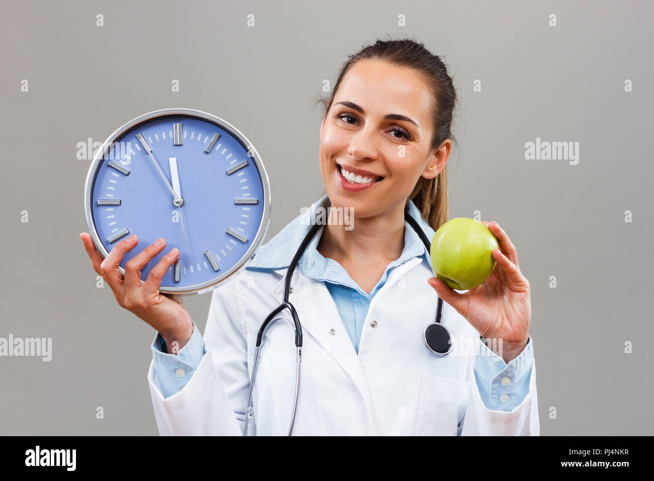 Beautiful female doctor is holding apple and clock to remind us how is ...