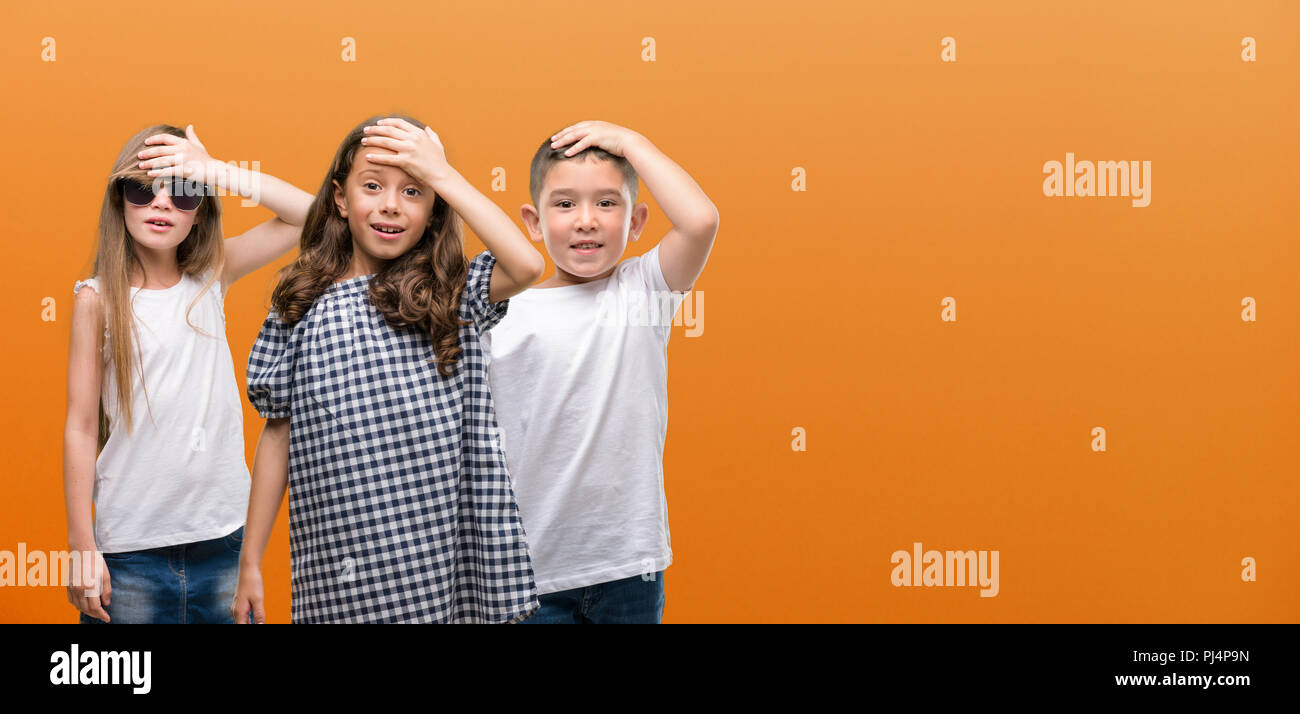 Group of boy and girls kids over orange background stressed with hand ...