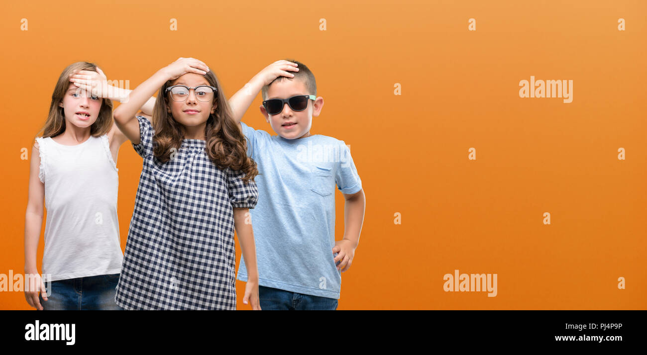 Group of boy and girls kids over orange background stressed with hand ...