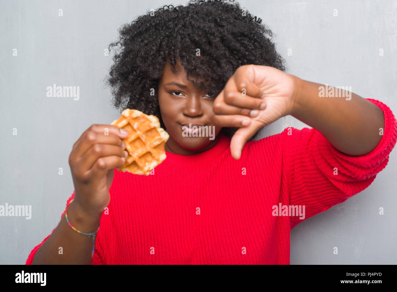 Young african american woman over grey grunge wall eating belgium ...