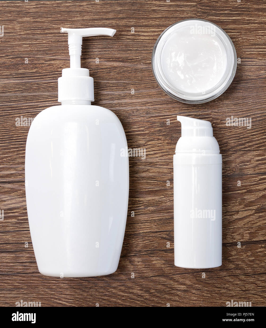 White cosmetic containers and open glass jar with cream on wooden ...