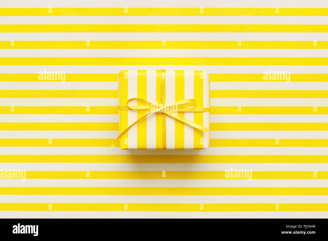 Yellow gift box on white & yellow striped wrapping paper. Minimal ...