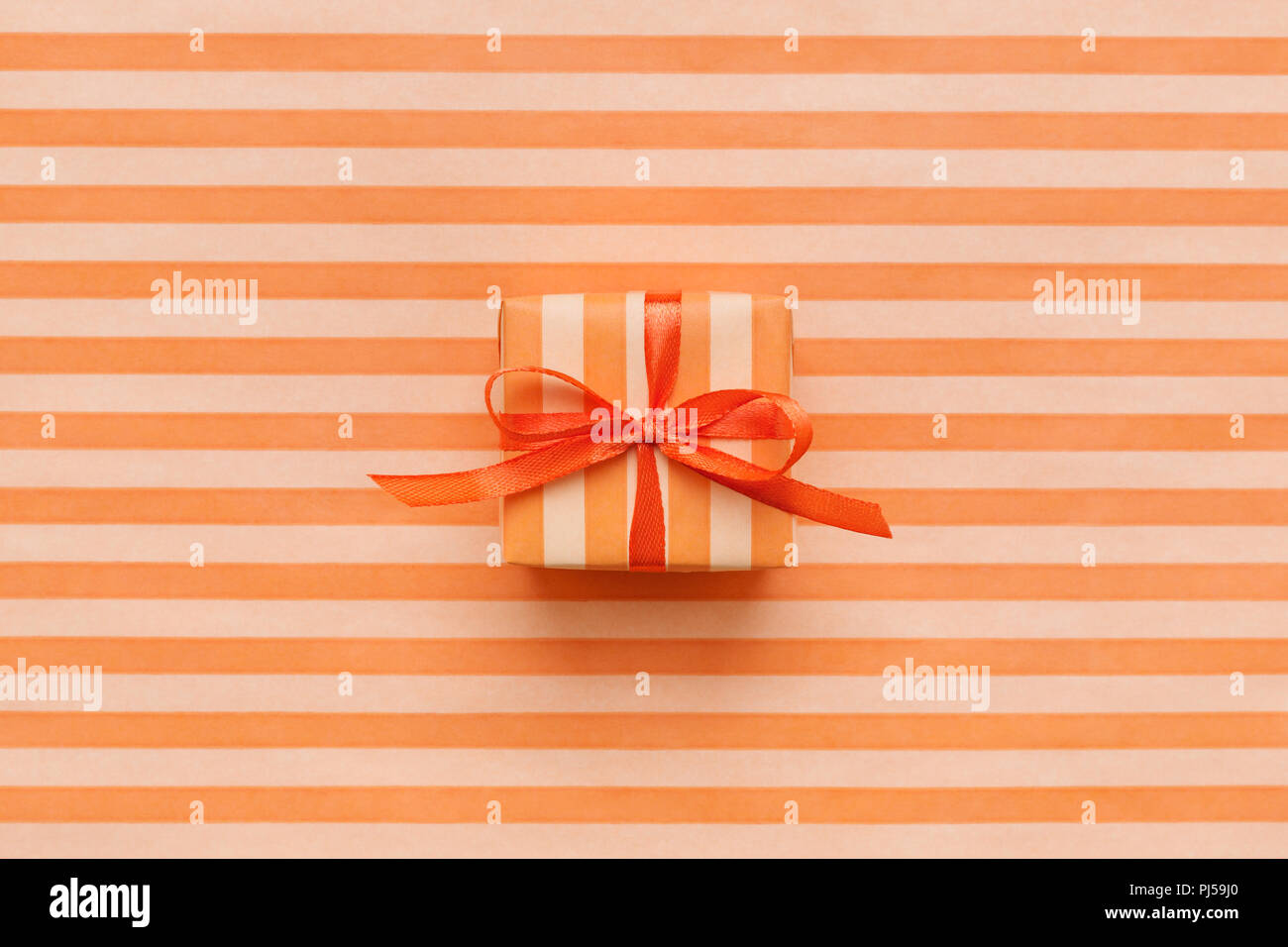 Orange color gift box on orange striped wrapping paper. Minimal ...