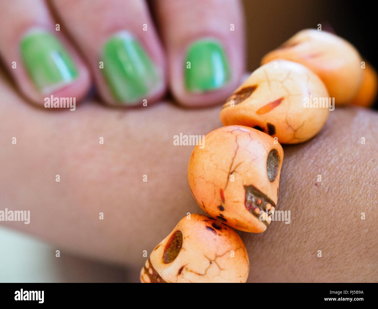 orange skull bracelet on green nailed woman arm Stock Photo - Alamy