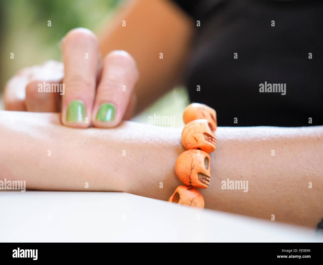 orange skull bracelet on green nailed woman arm Stock Photo - Alamy