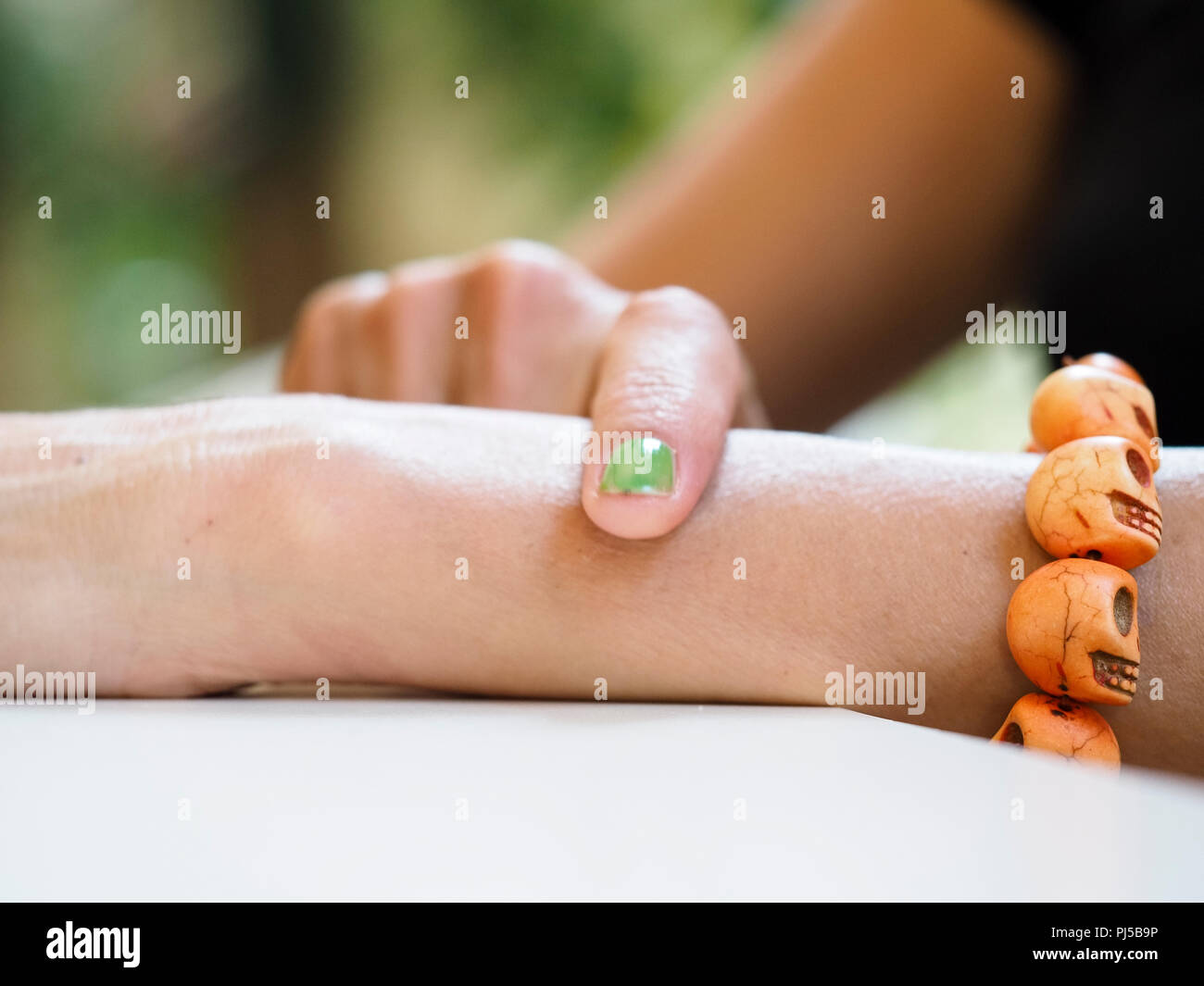 orange skull bracelet on green nailed woman arm Stock Photo - Alamy