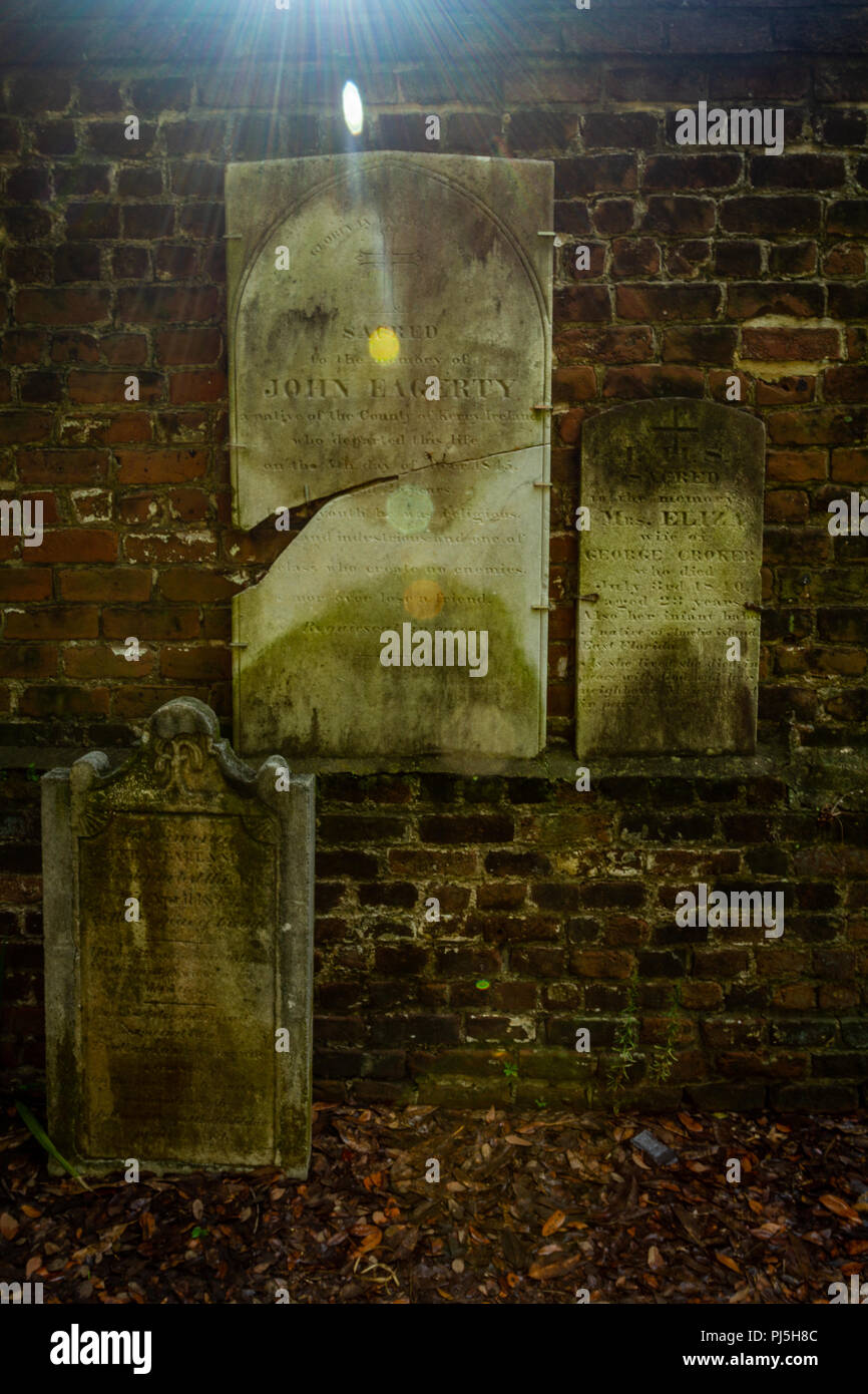 A row of headstones line a brick wall in a cemetery Stock Photo - Alamy