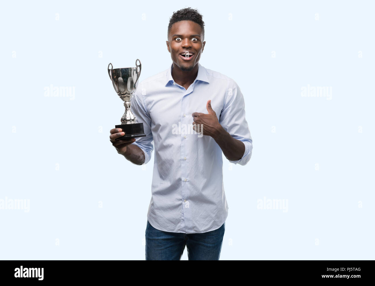 Young african american man holding trophy with surprise face pointing ...