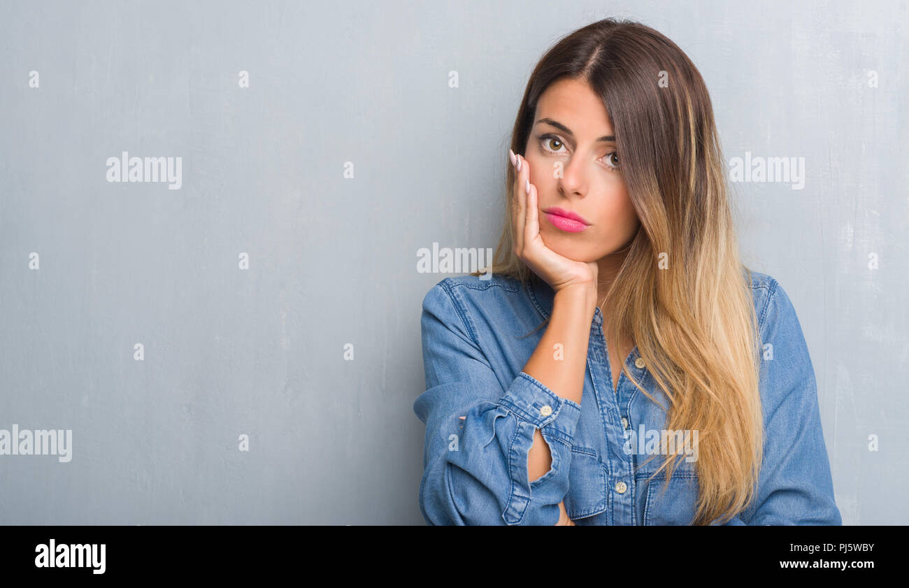 Young adult woman over grunge grey wall wearing denim outfit thinking ...