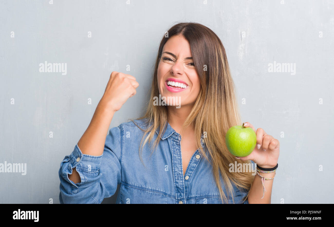 Young adult woman over grey grunge wall eating fresh green apple ...