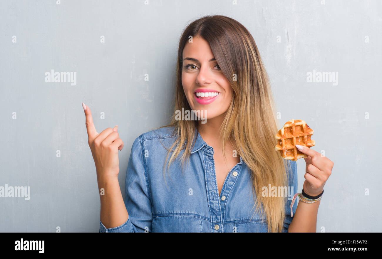 Young adult woman over grey grunge wall eating Belgium waffle very ...