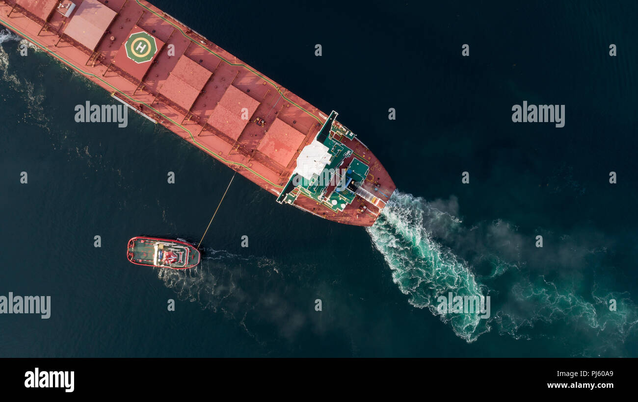 Aerial shot of a cargo ship approaching port with help of towing ship ...
