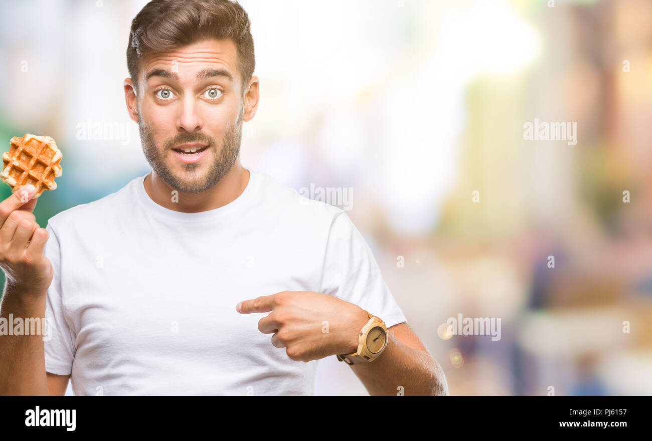 Young handsome man eating a sweet waffle over isolated background with ...