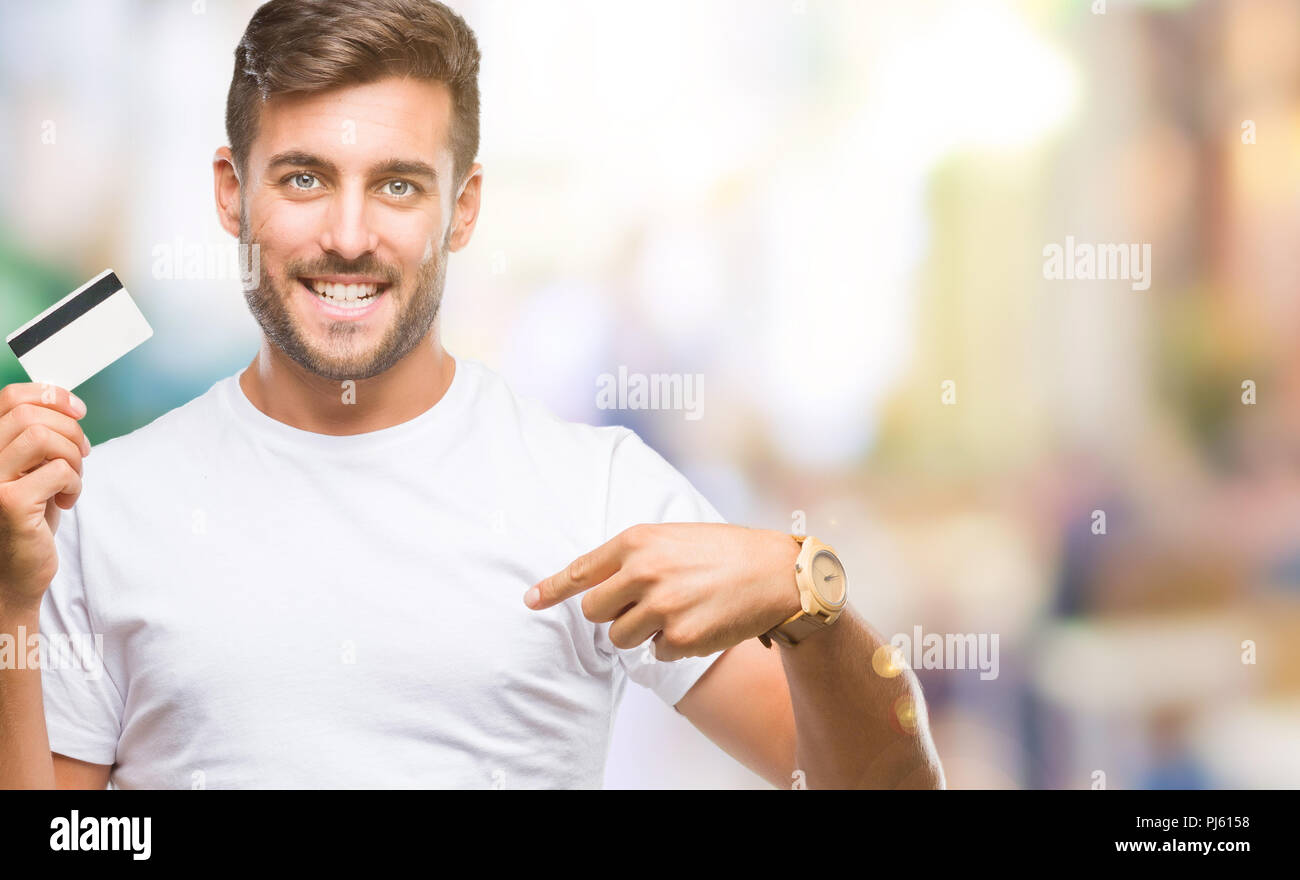 Young handsome man holding credit card over isolated background with ...