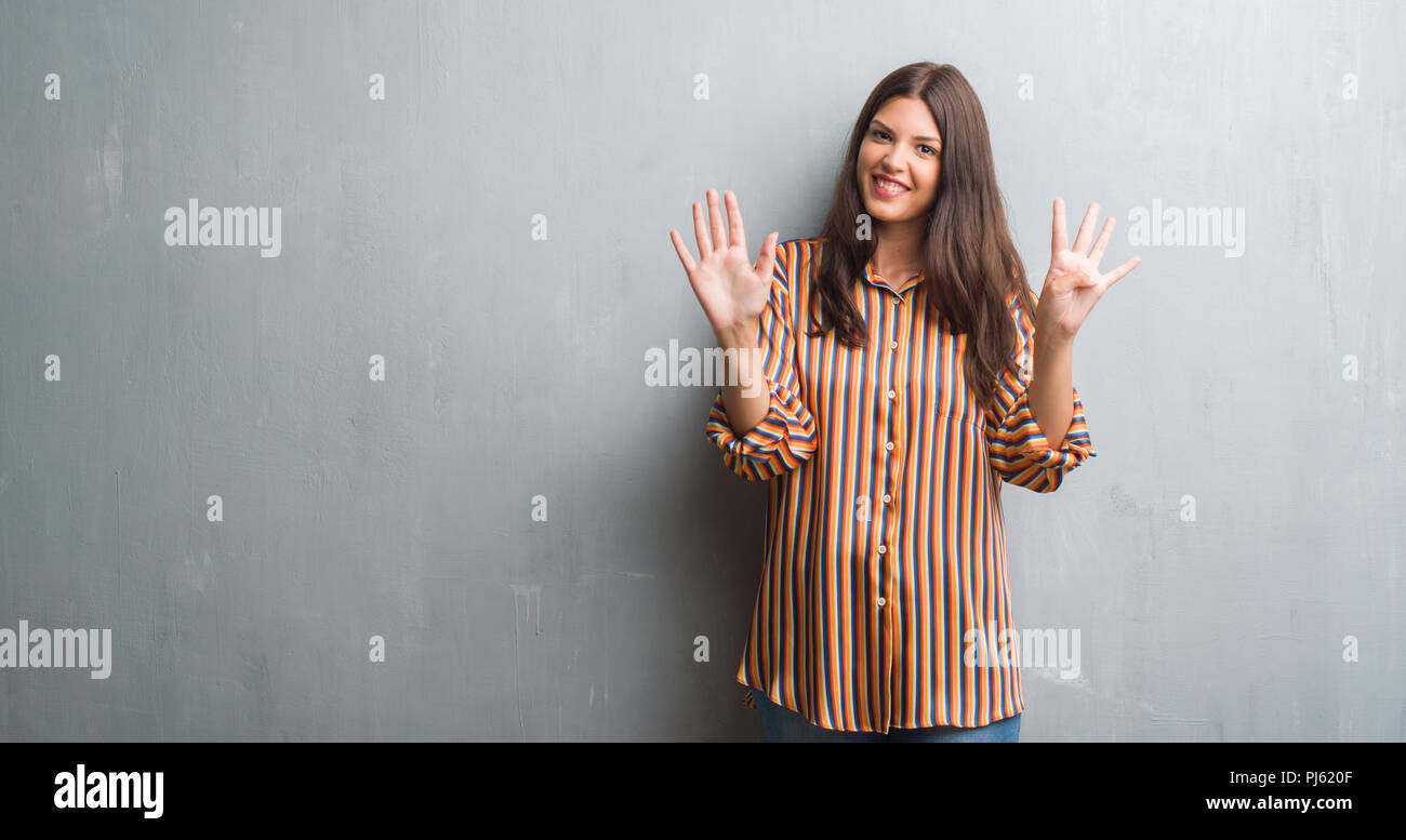 Young brunette woman over grunge grey wall showing and pointing up with ...