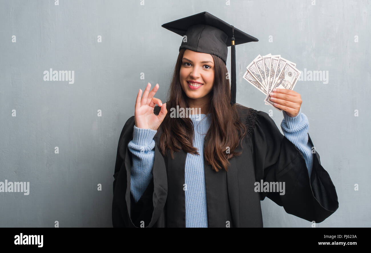 Young brunette woman over grunge grey wall wearing graduate uniform ...
