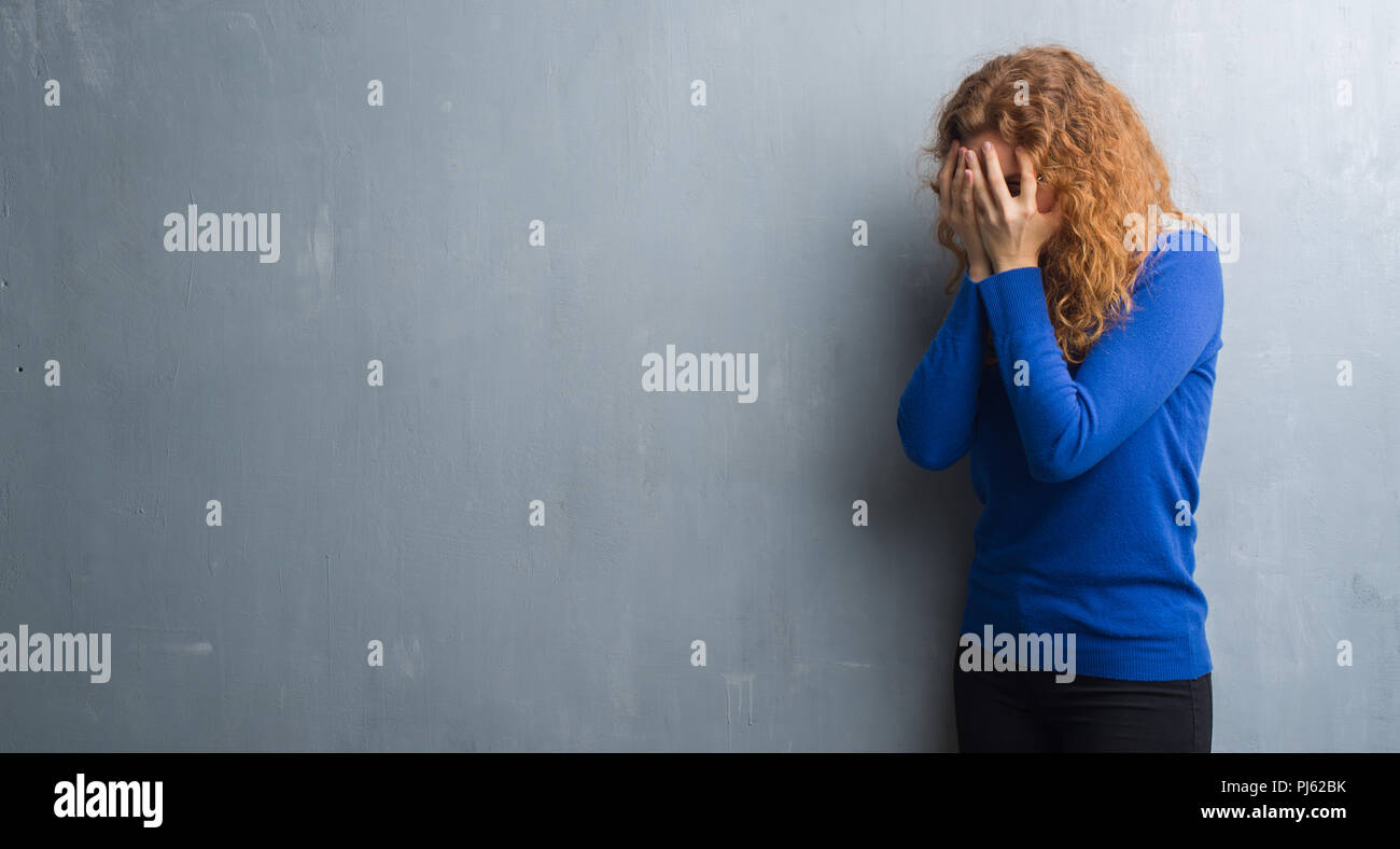 Young redhead woman over grey grunge wall with sad expression covering ...