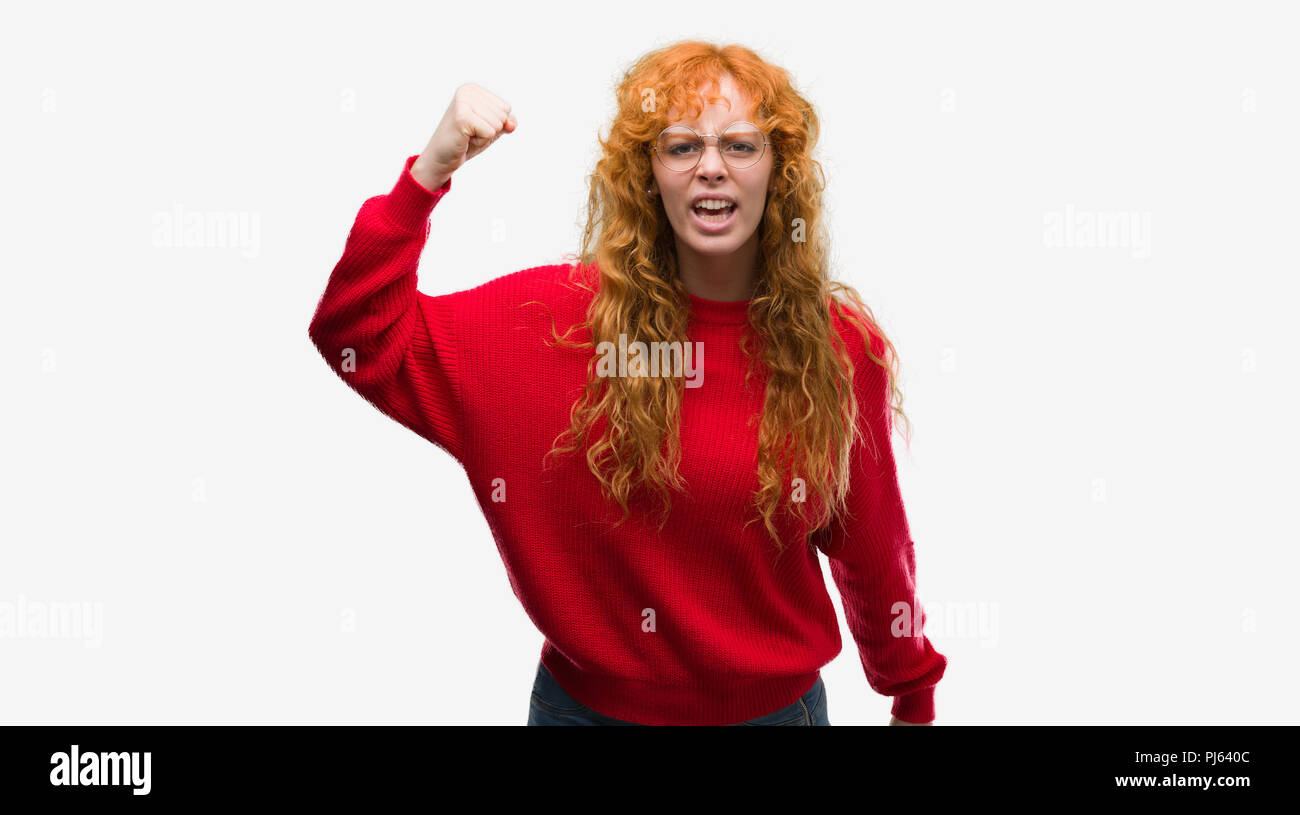 Young redhead woman wearing red sweater angry and mad raising fist ...