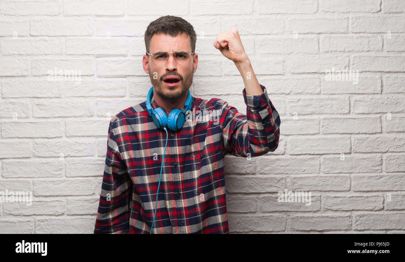 Young adult man over brick wall wearing headphones annoyed and ...