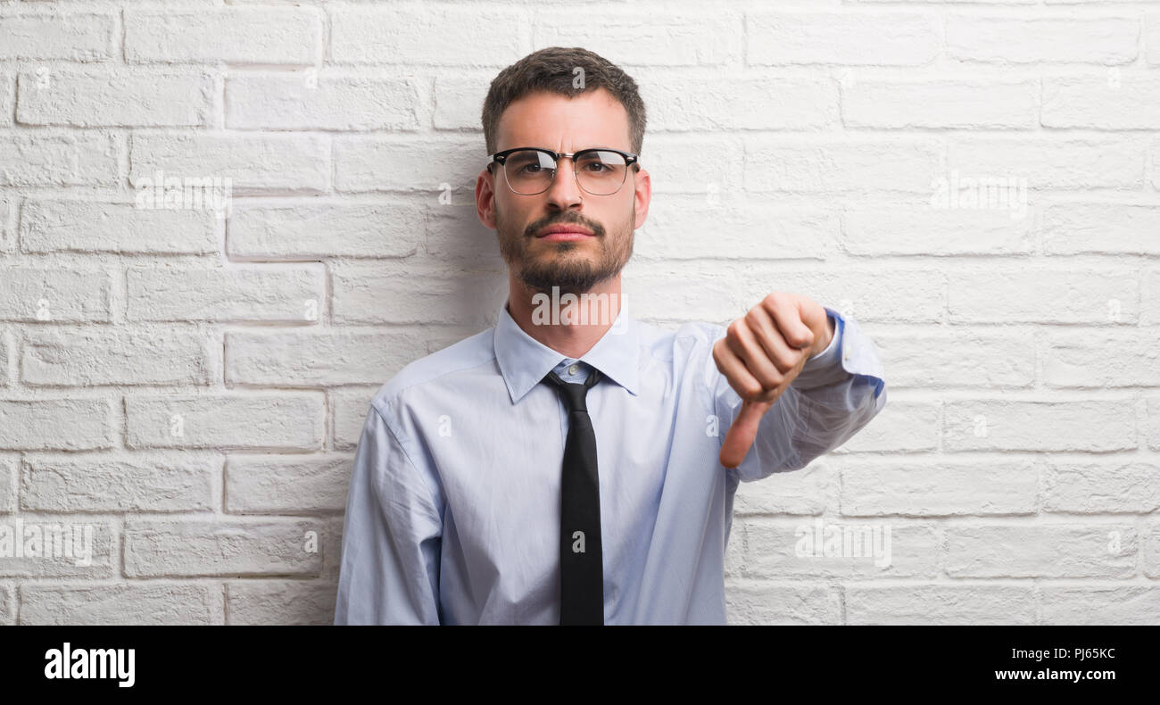 Young adult business man standing over white brick wall with angry face ...