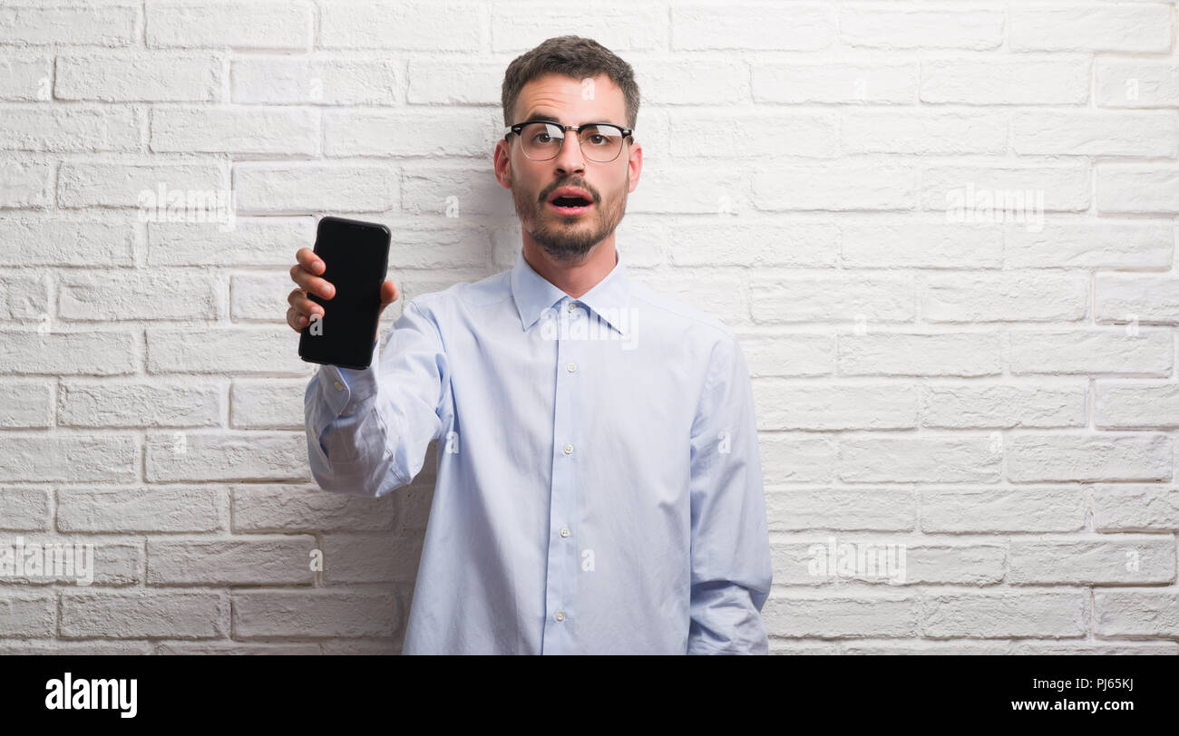 Young adult man talking on the phone standing over white brick wall ...