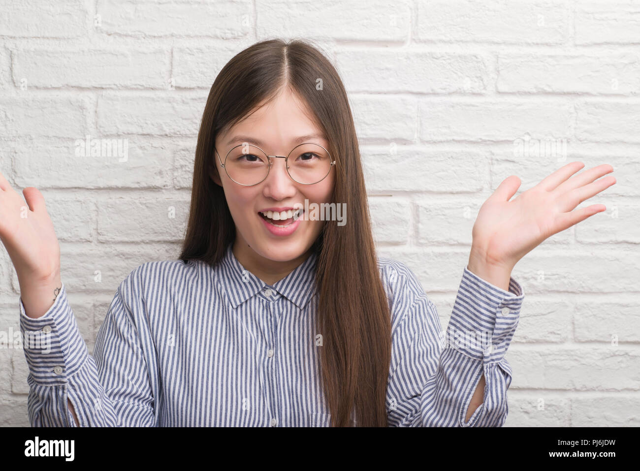 Young Chinese business woman over brick wall very happy and excited ...