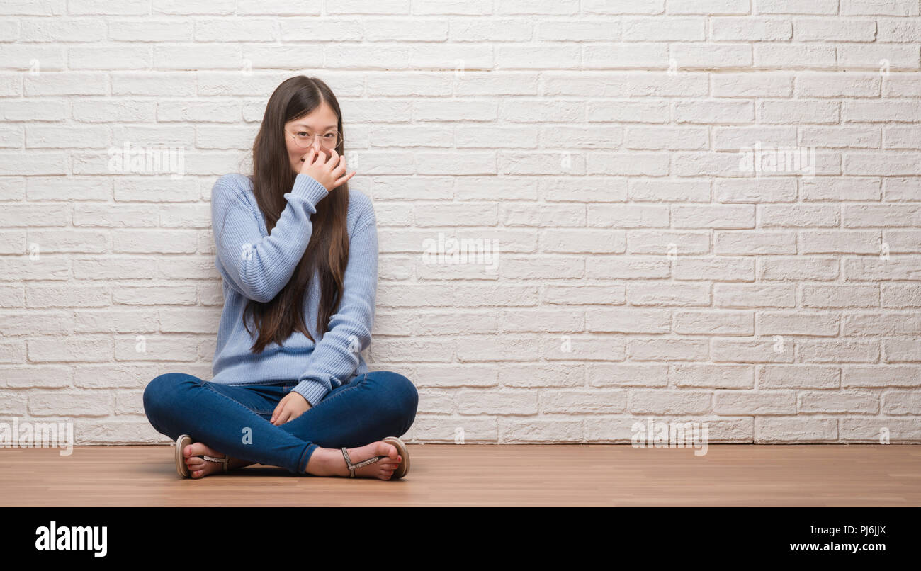 Young Chinese woman sitting on the floor over brick wall smelling ...