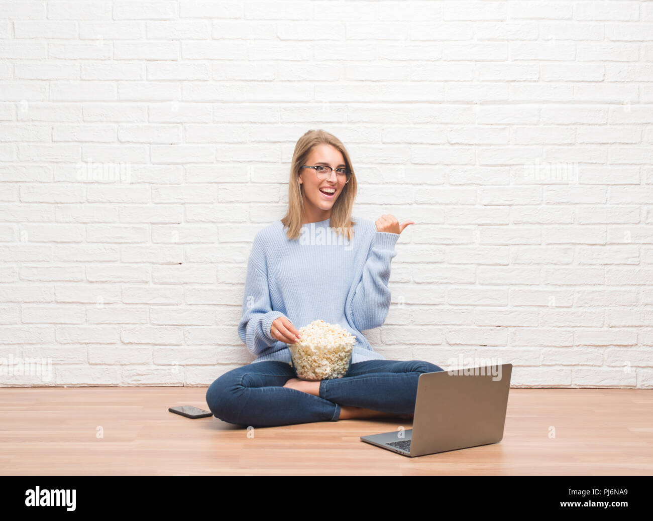 Beautiful woman sitting on the floor eating popcorn and watching a ...