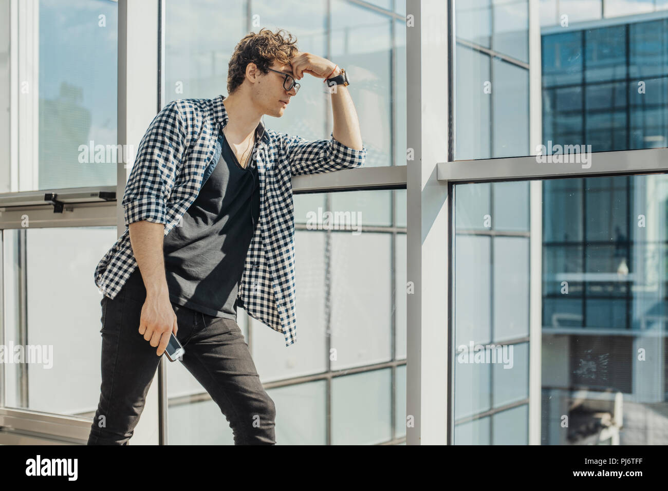 Distant plan of young man standing next to big windows at metro station ...
