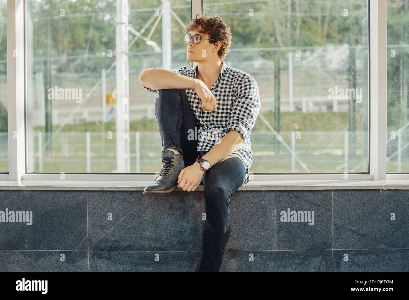 Distant plan of young man sitting next to big windows at metro station ...