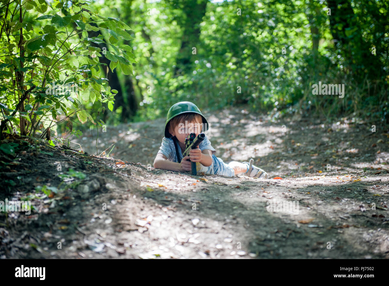 funny little caucasian boy in military helmet hiding behind trees with ...