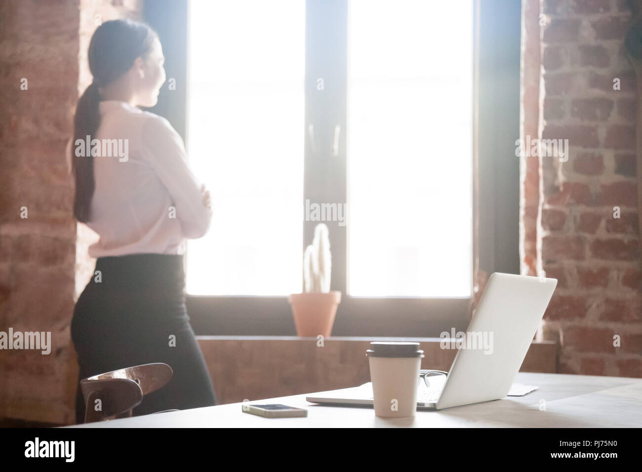Young woman looking out window in office Stock Photo - Alamy