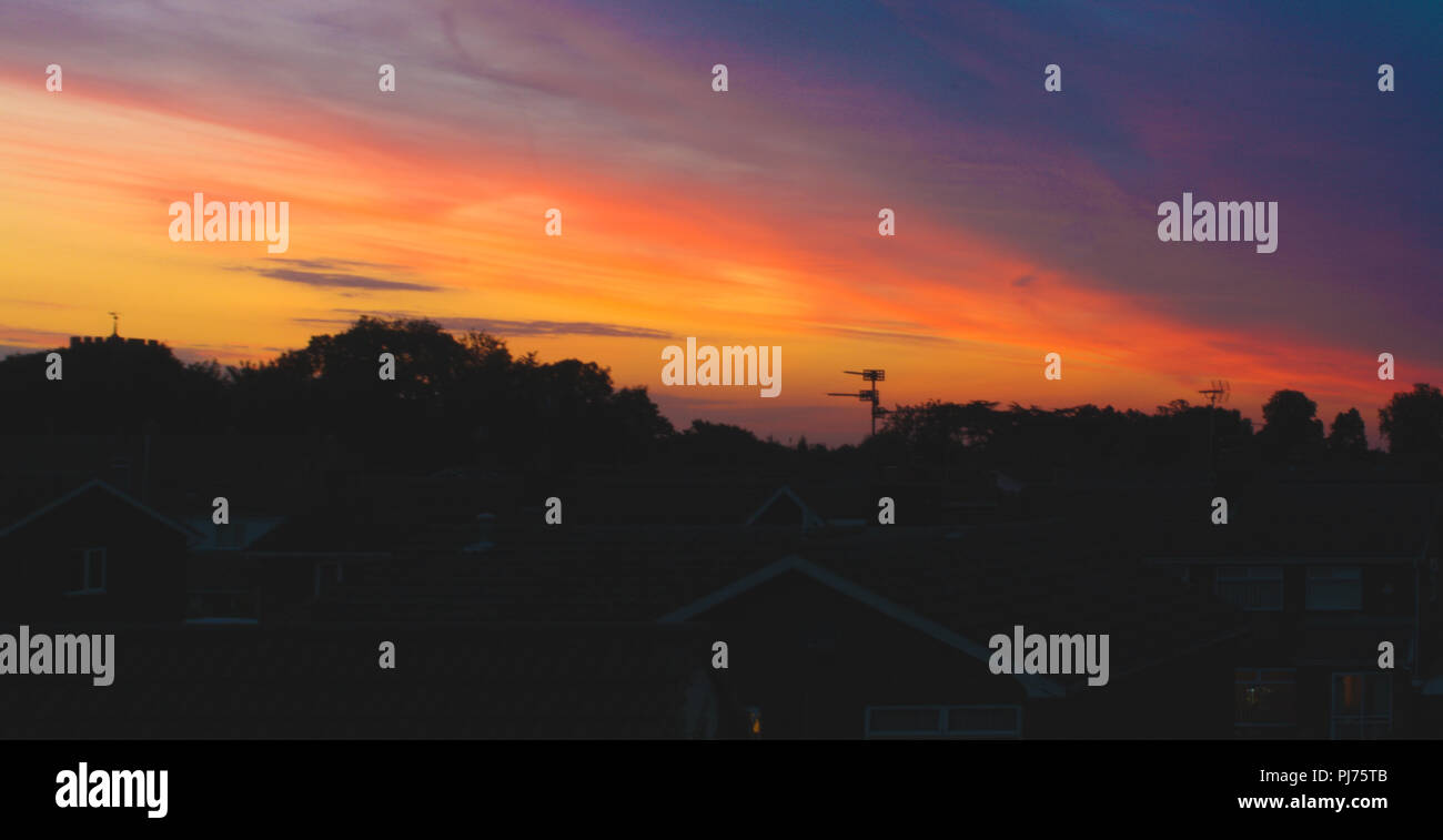 Sunset captured over village with silhouetted treeline below Stock ...