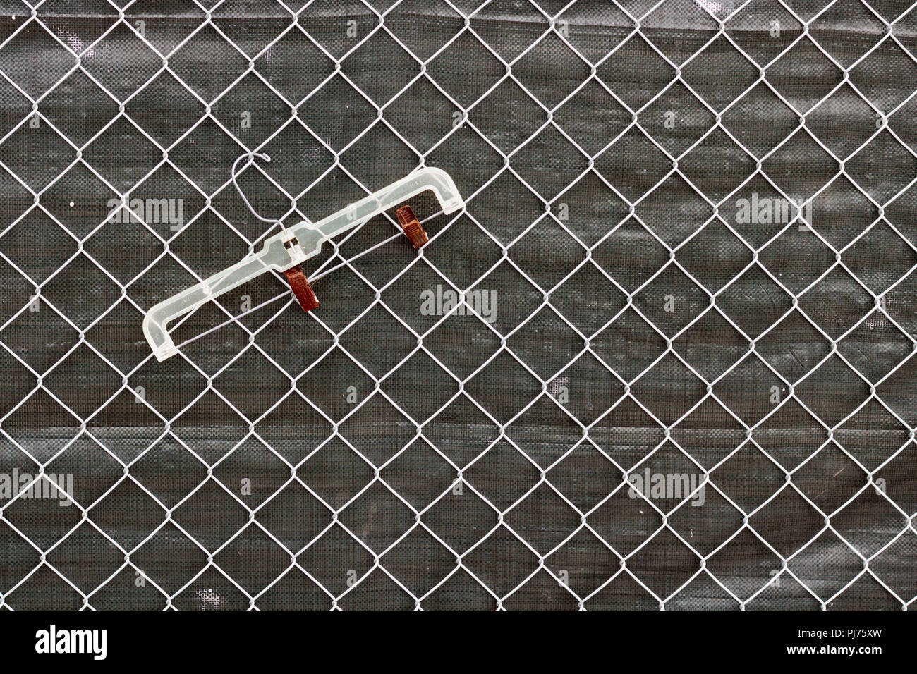 Rusty plastic garment hanger hanging on chain link fence with a gray ...