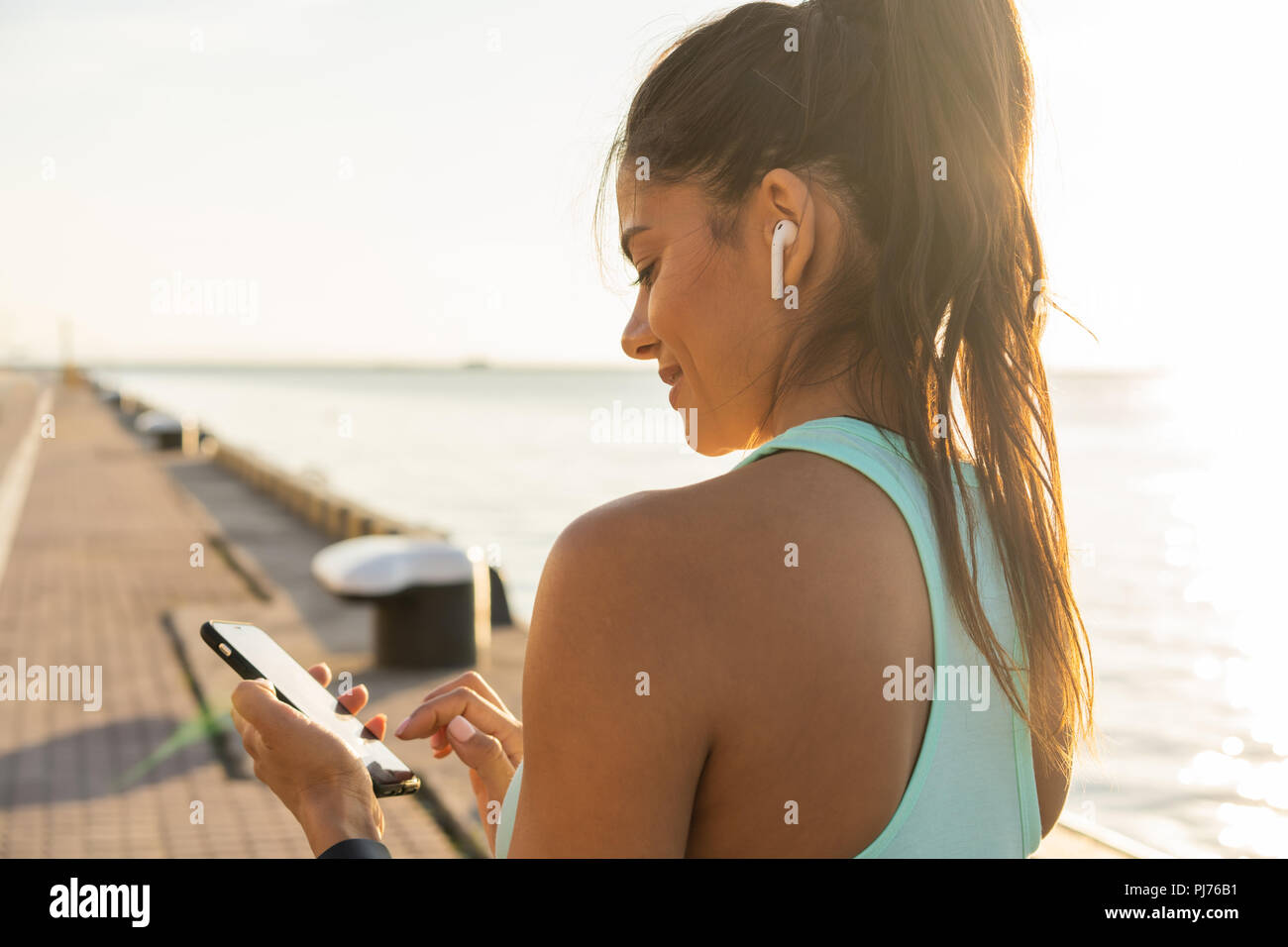 Tired fitness woman sweating taking a break listening to music on phone ...