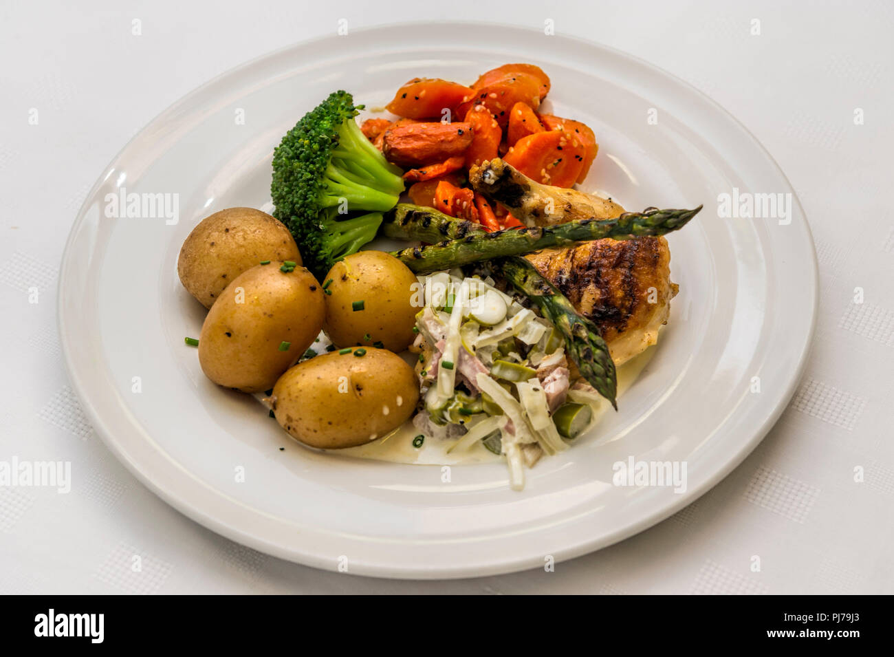 Portion of roast chicken on white plate with selection of seasonal ...