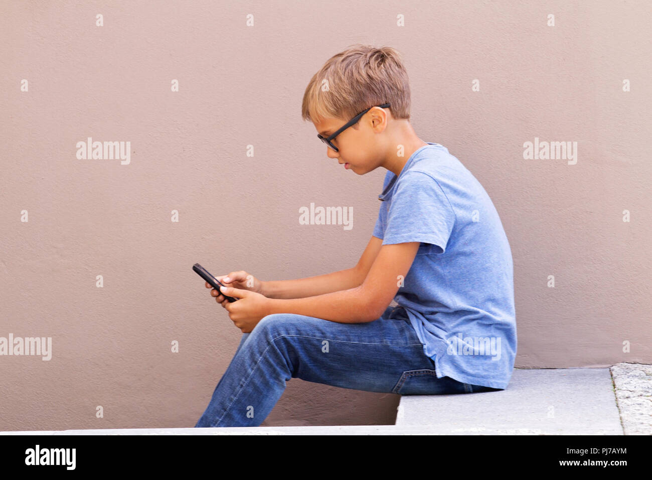 Boy with smartphone sitting on stairs outdoor. Kid wathing to screen ...