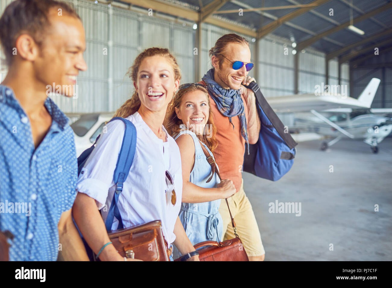 Happy friends walking in airplane hangar Stock Photo - Alamy
