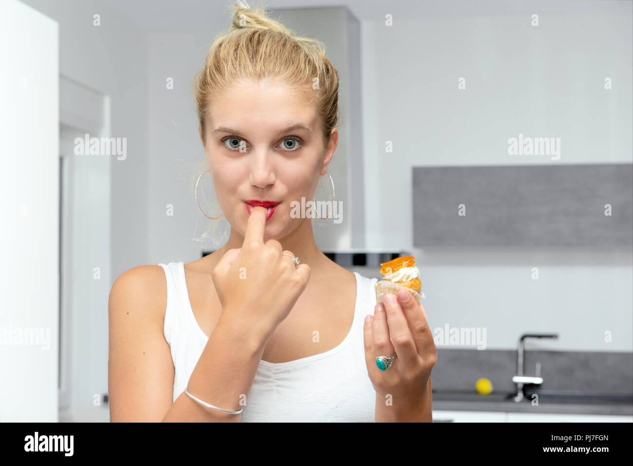 a pretty young blond woman eating cakes in the kitchen Stock Photo - Alamy