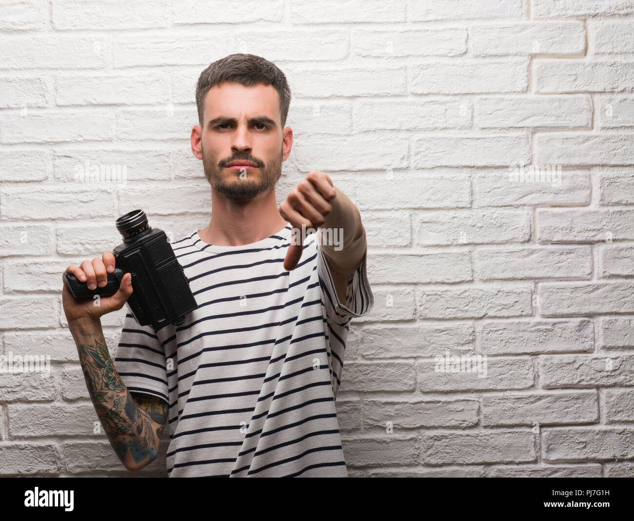 Young man filming holding video camera standing over white brick wall ...