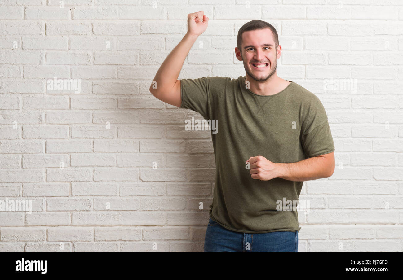 Young caucasian man standing over white brick wall angry and mad ...