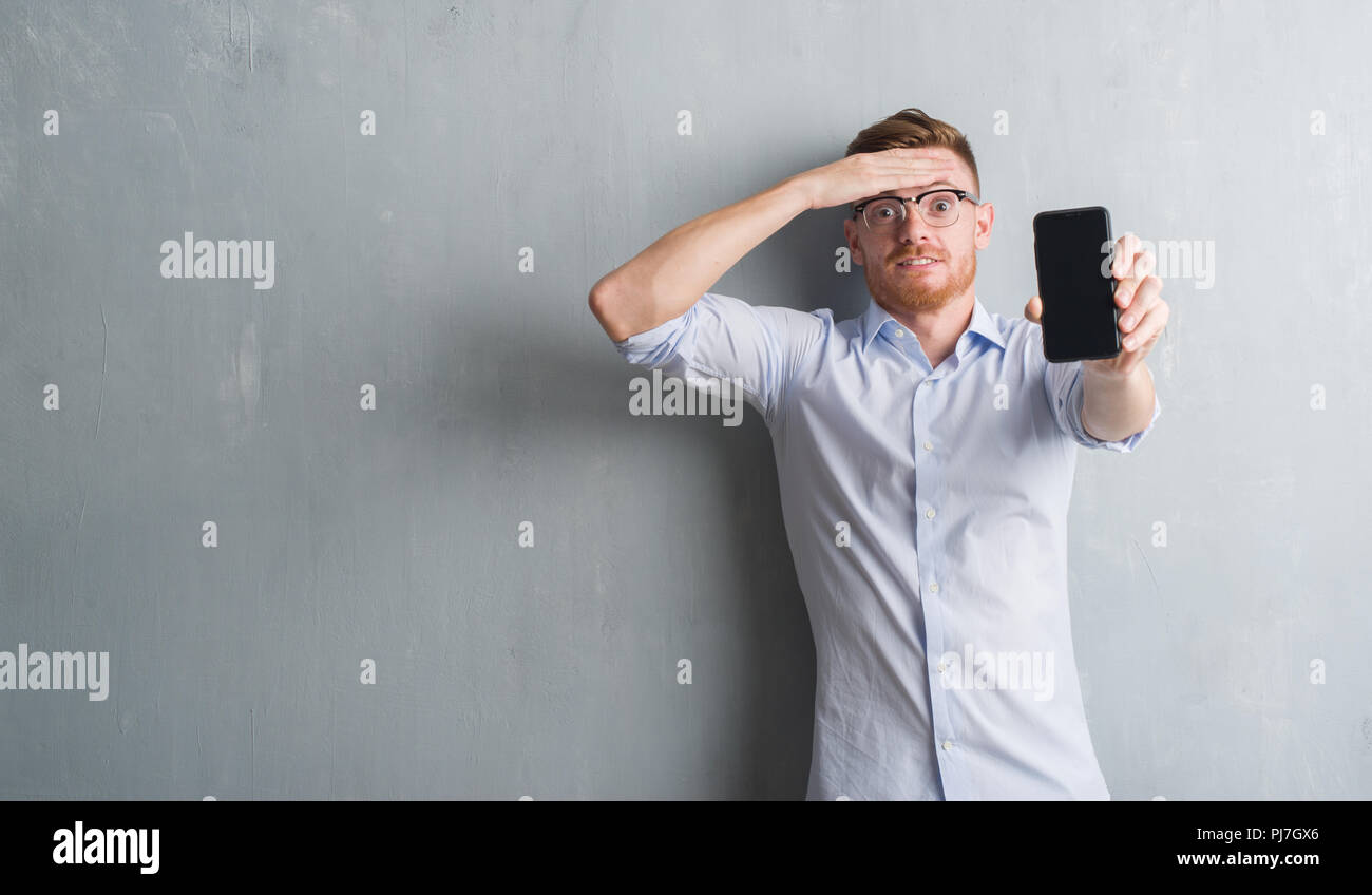 Young redhead man over grey grunge wall showing blank screen of ...