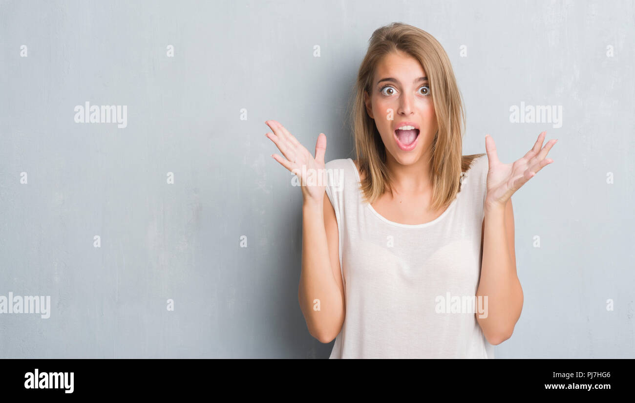Beautiful young woman standing over grunge grey wall very happy and ...