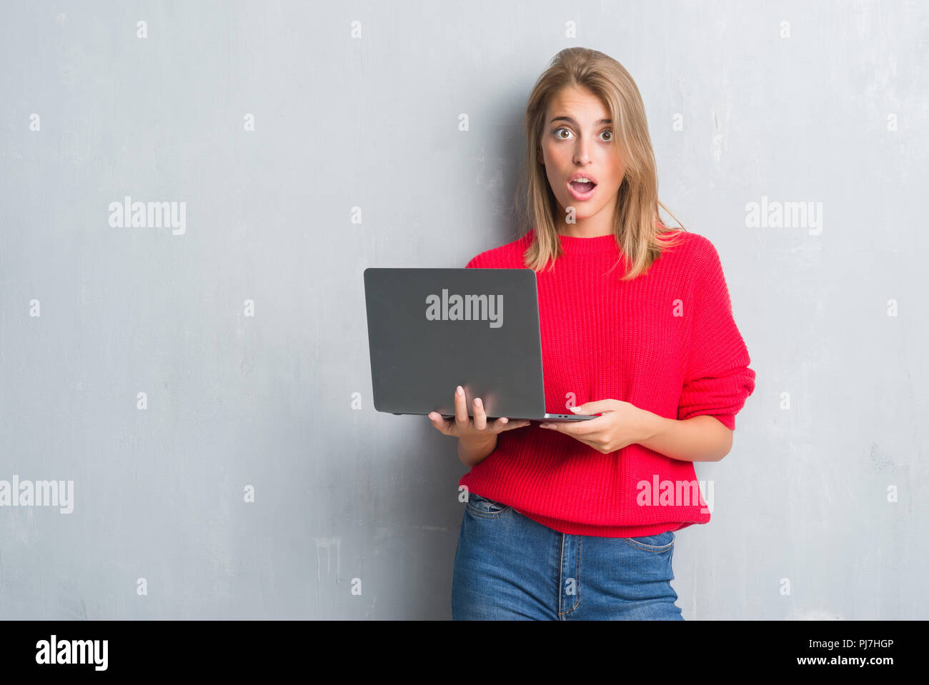 Beautiful young woman over grunge grey wall using computer laptop ...