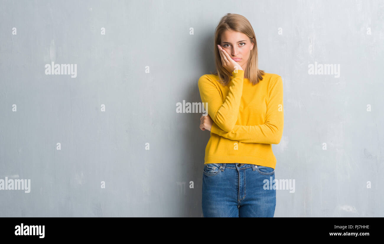 Beautiful young woman standing over grunge grey wall thinking looking ...