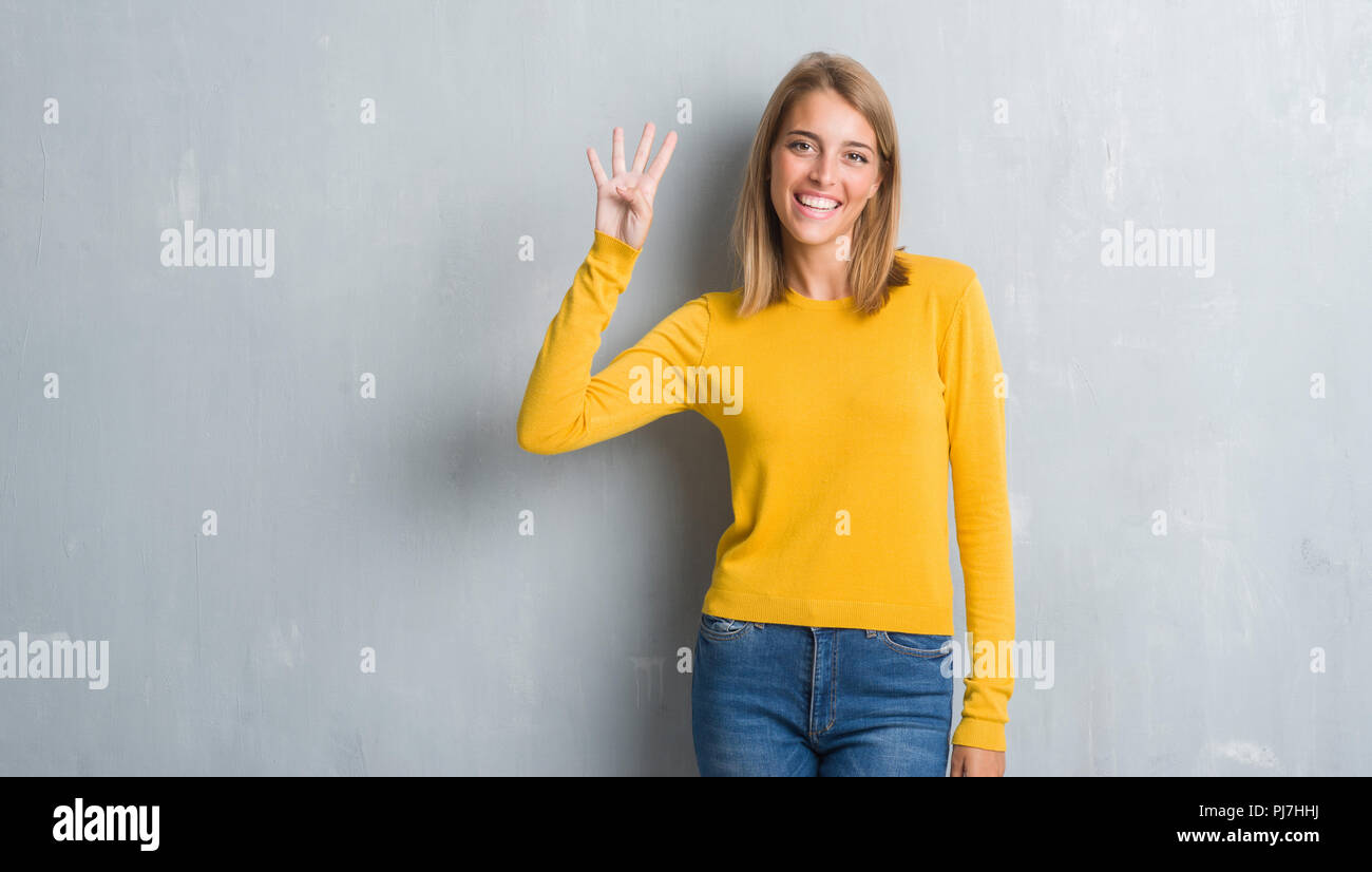 Beautiful young woman standing over grunge grey wall showing and ...