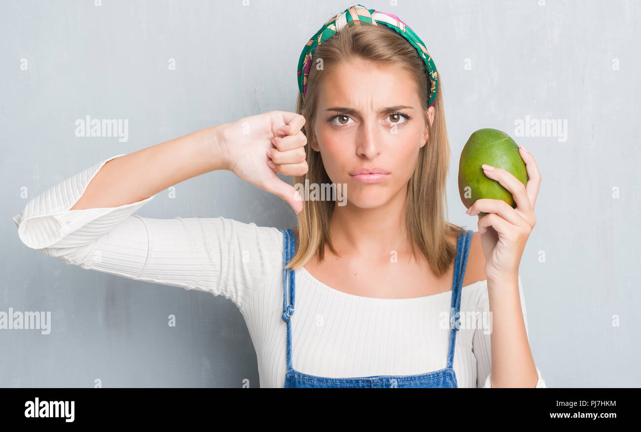 Beautiful young woman over grunge grey wall holding fresh mango with ...