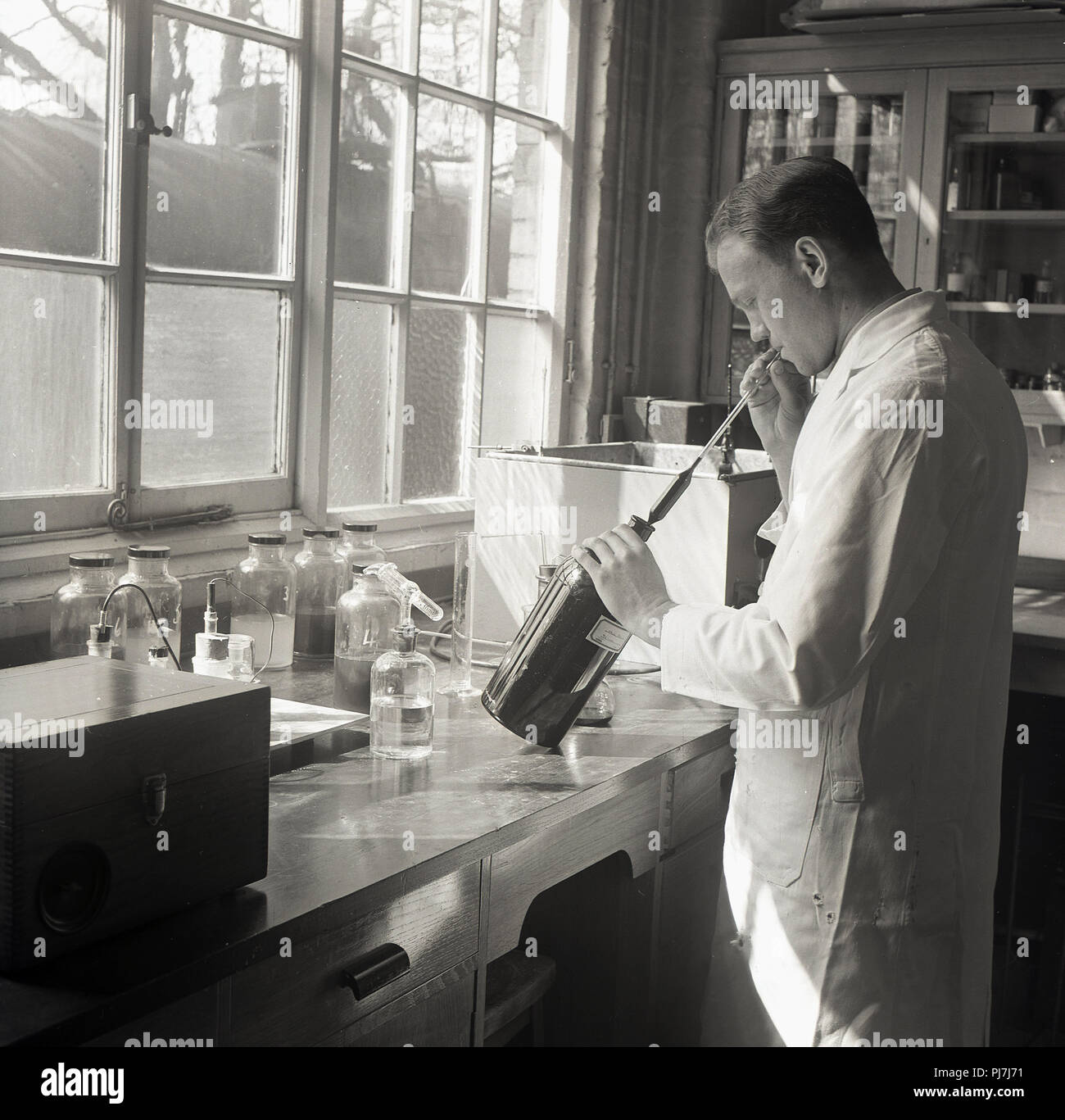 1950s, a white-coated scientis working in a factory laboratory a the ...